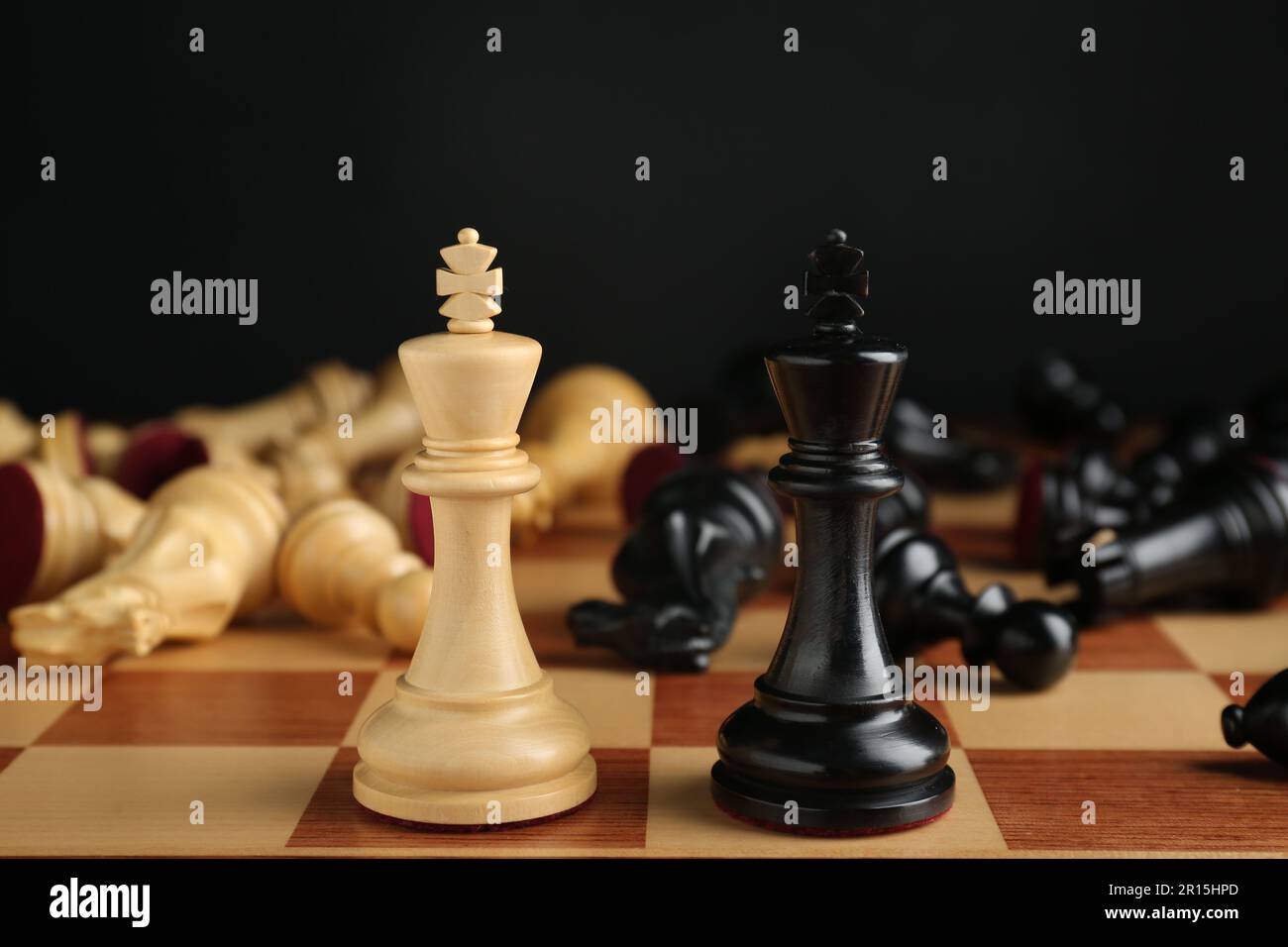Kings among fallen chess pieces on chessboard against black background ...