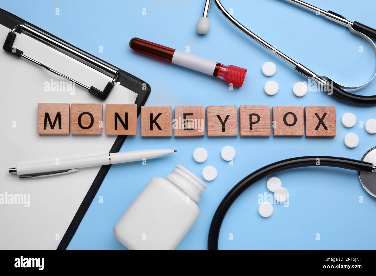 Word Monkeypox made of wooden cubes, test tube and pills on light blue ...