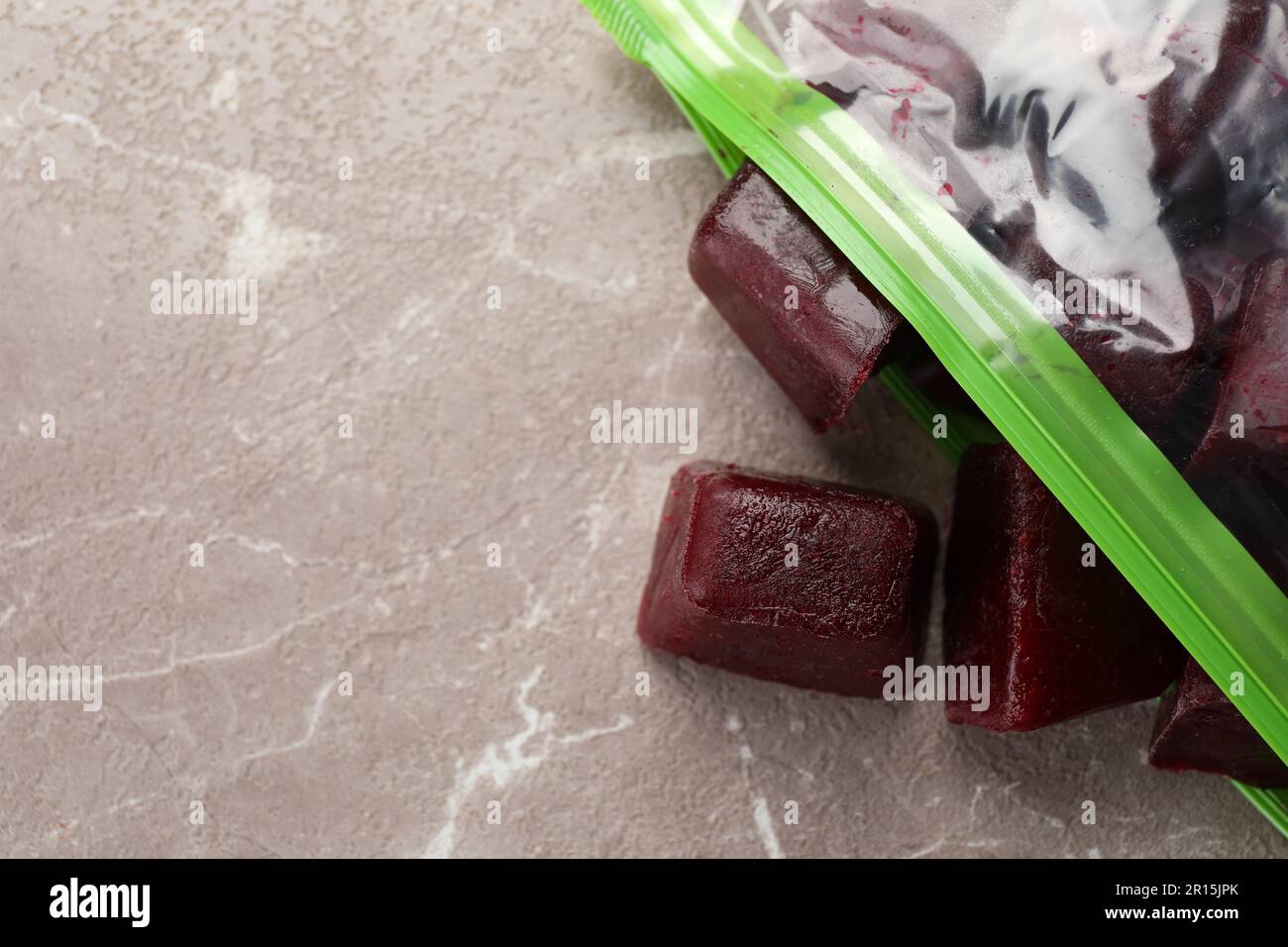 Frozen beet puree cubes in plastic bag on marble table, top view. Space ...