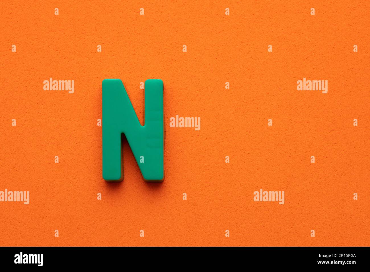 Alphabet letter N - Green plastic piece on orange foamy background ...