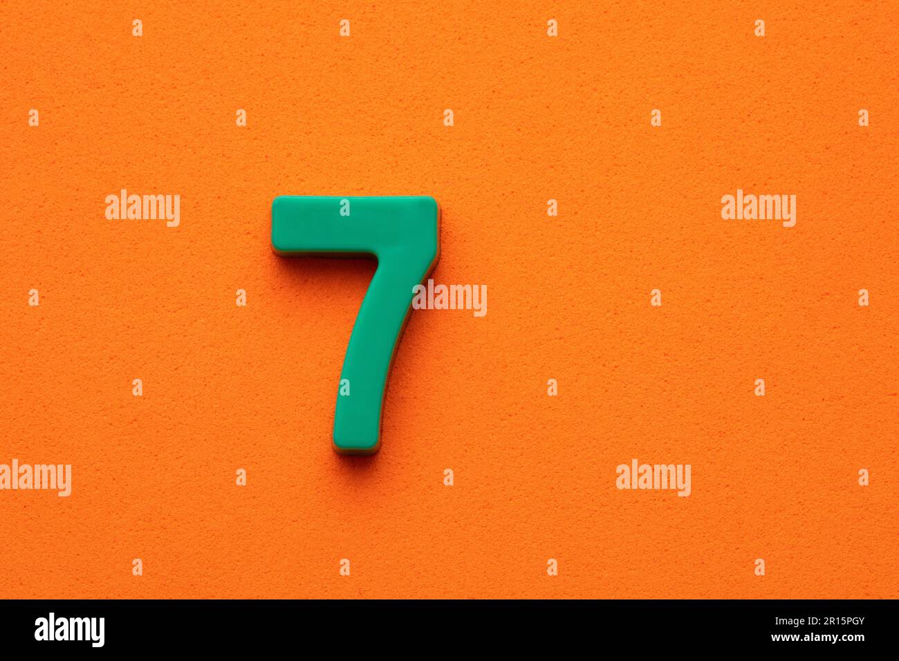 Green plastic number seven - plastic digit on orange foamy background ...