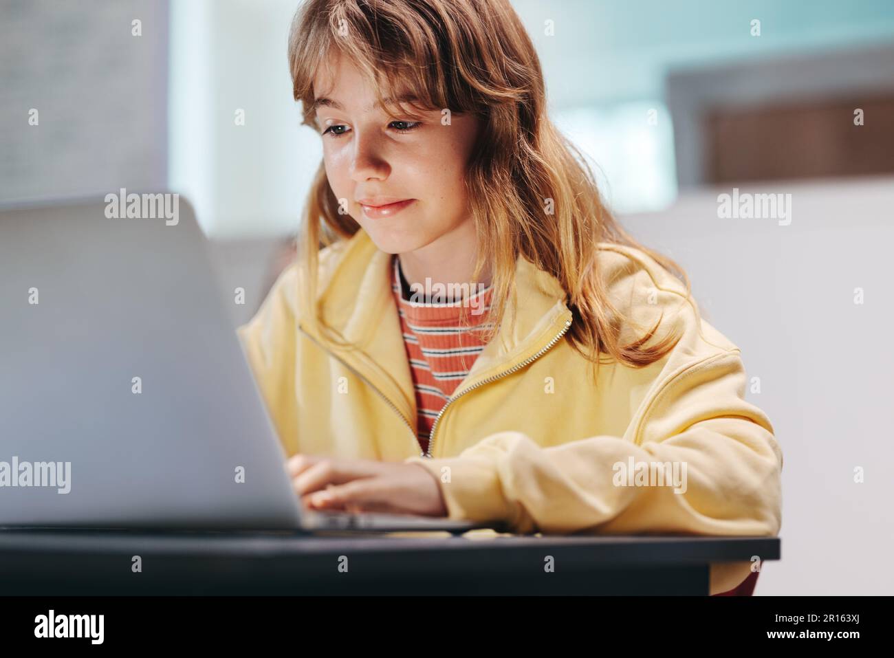 Child sitting with a laptop in a coding classroom, developing her innovative skills through ...