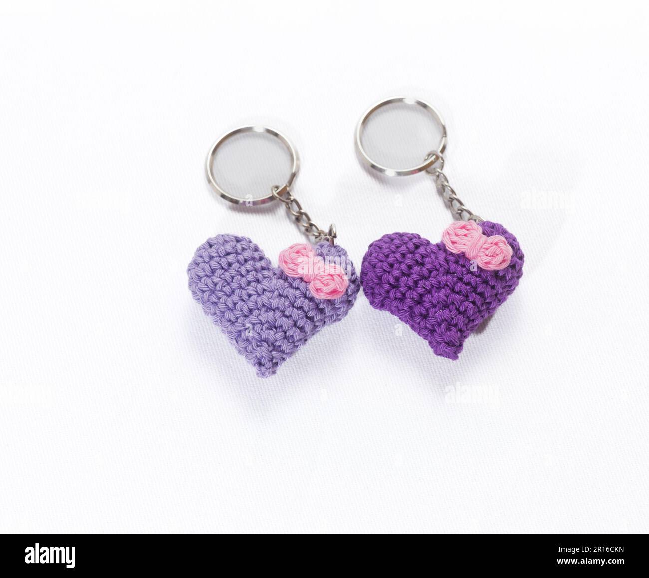 A pair of crocheted purple heart-shaped keyrings on a white background ...