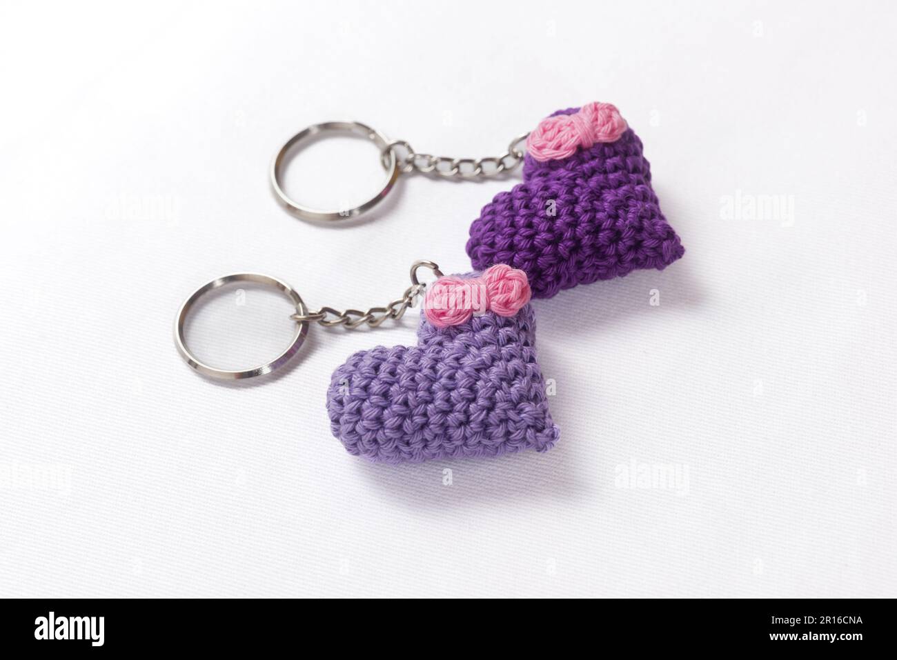 A pair of crocheted purple heart-shaped keyrings on a white background ...