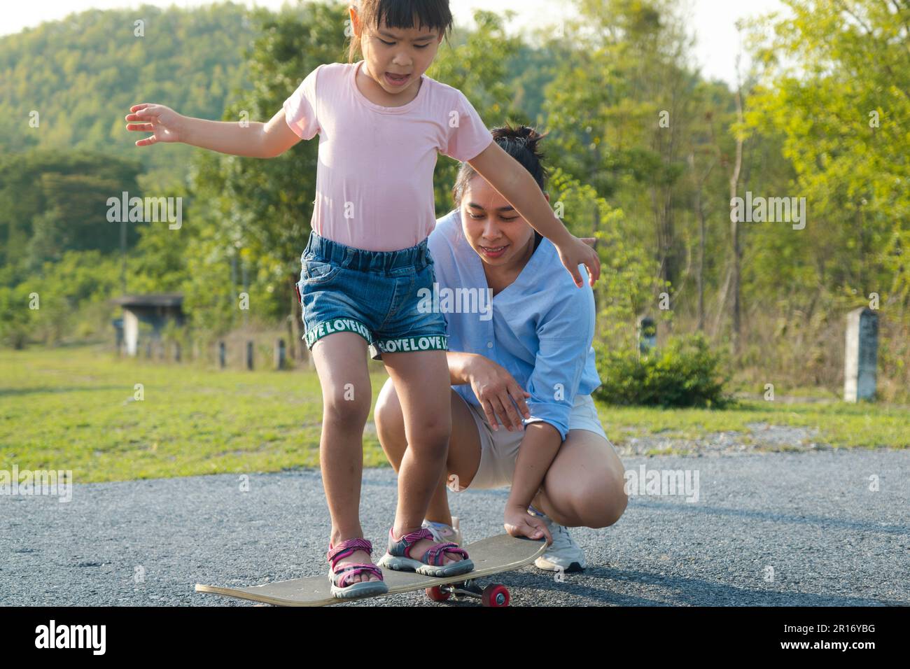 Mother teaching her daughter how to skateboard in the park. Child ...