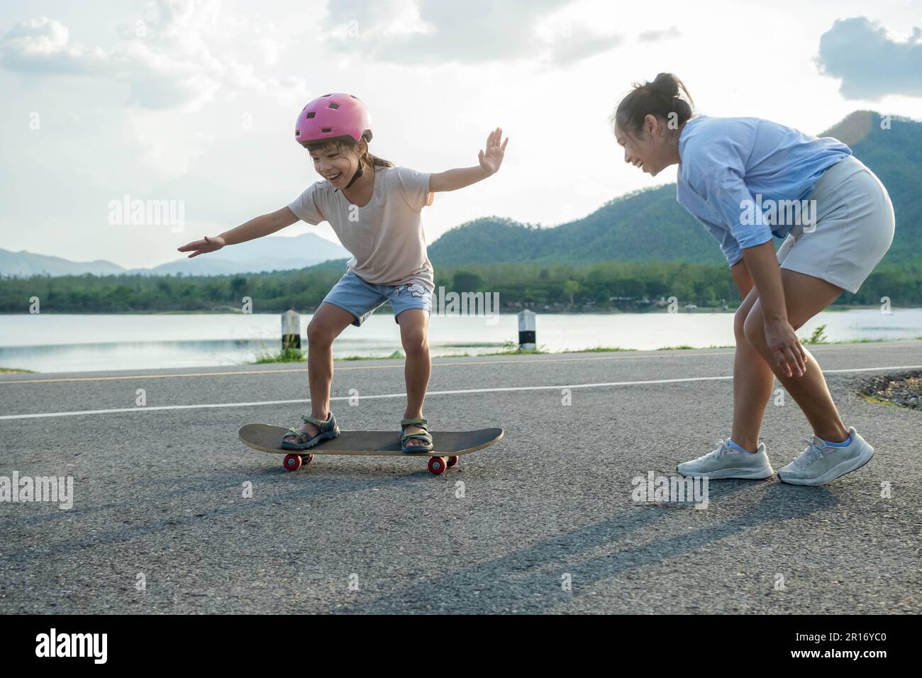 Mother teaching her daughter how to skateboard in the park. Child ...