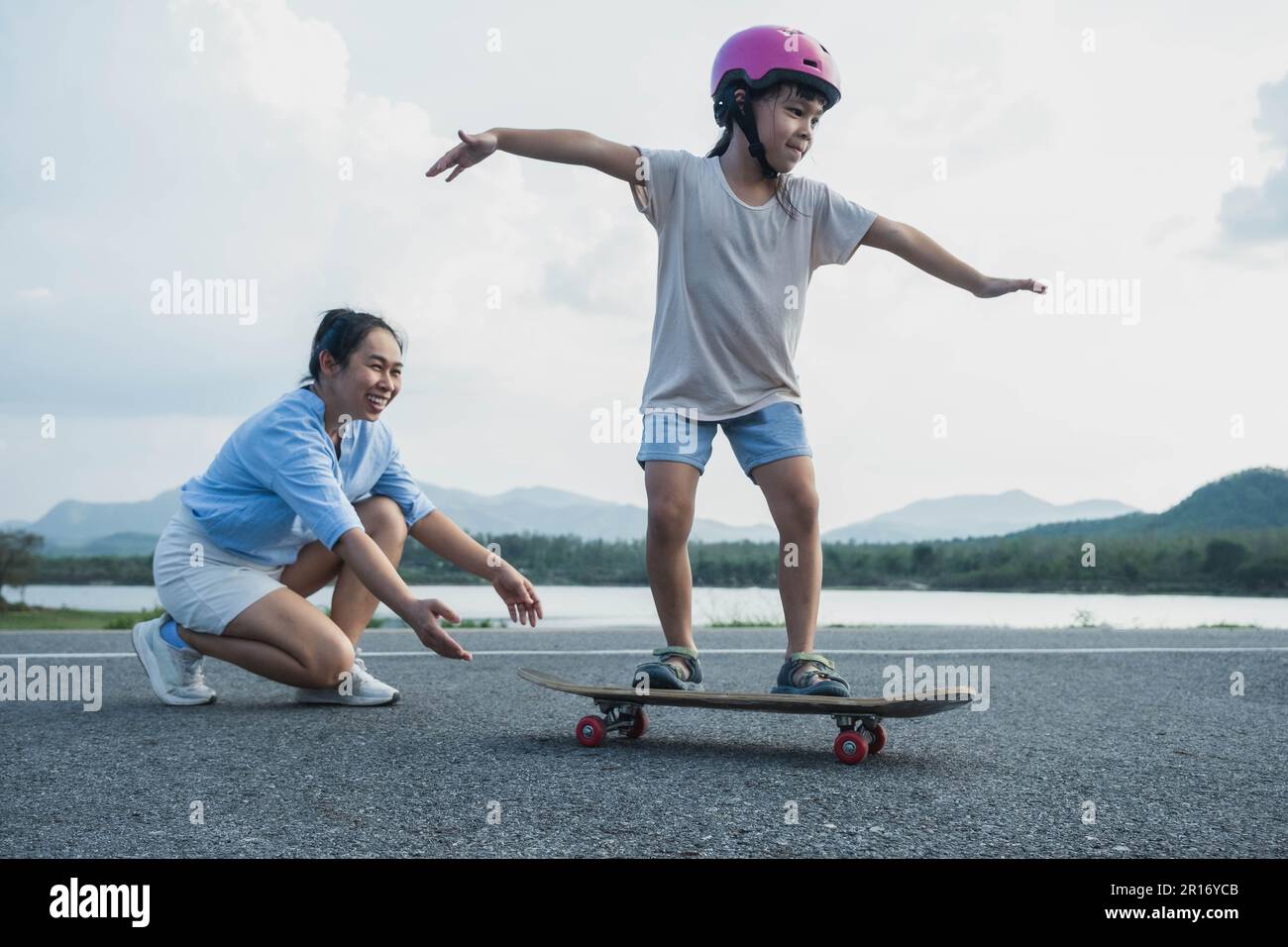 Mother teaching her daughter how to skateboard in the park. Child ...