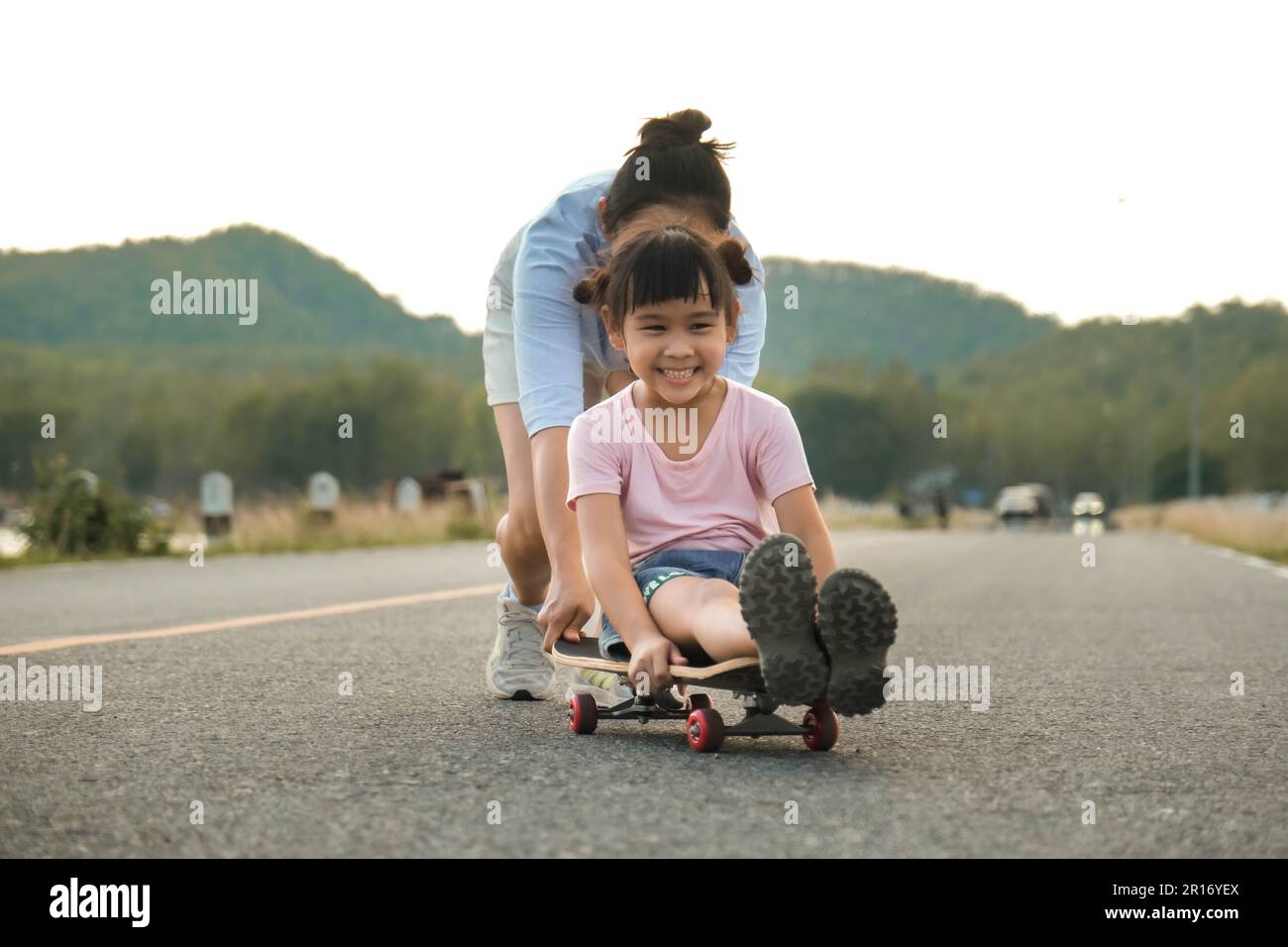 Mother teaching her daughter how to skateboard in the park. Child ...