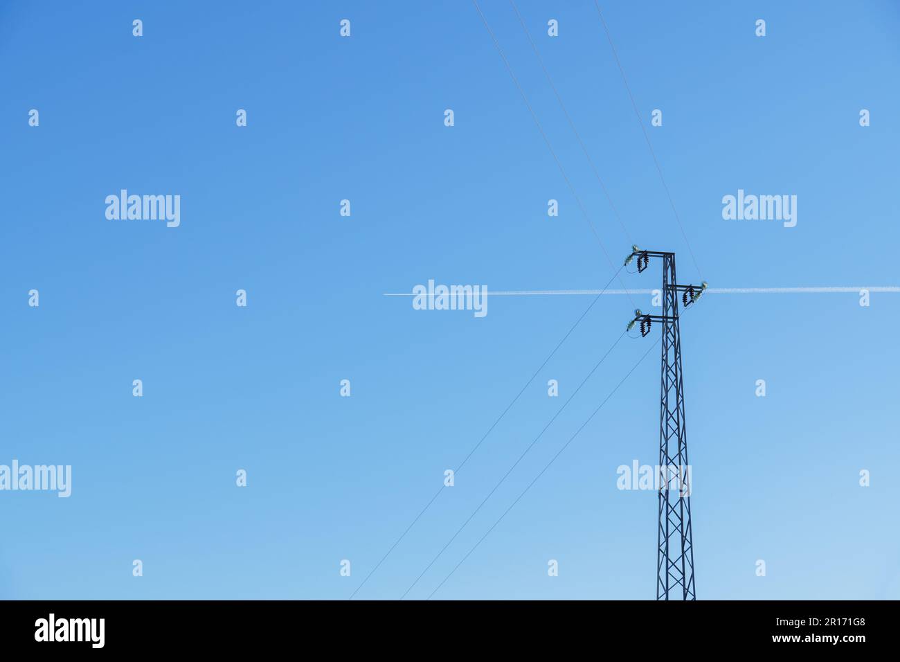 A plane passes leaving its wake behind a high-tension tower, in the ...