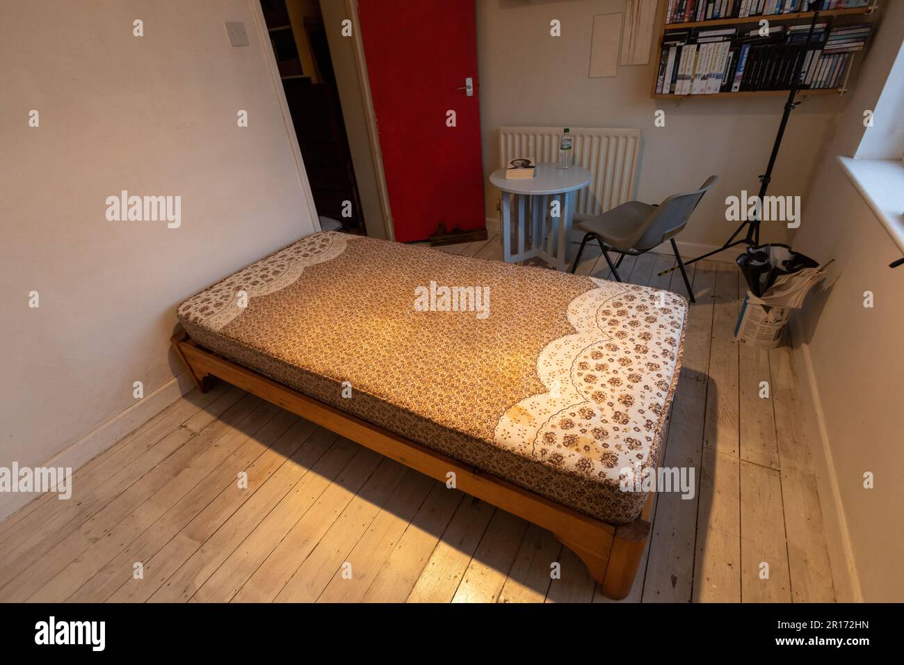 A wooden single bed in a small room with a red door white washed ...