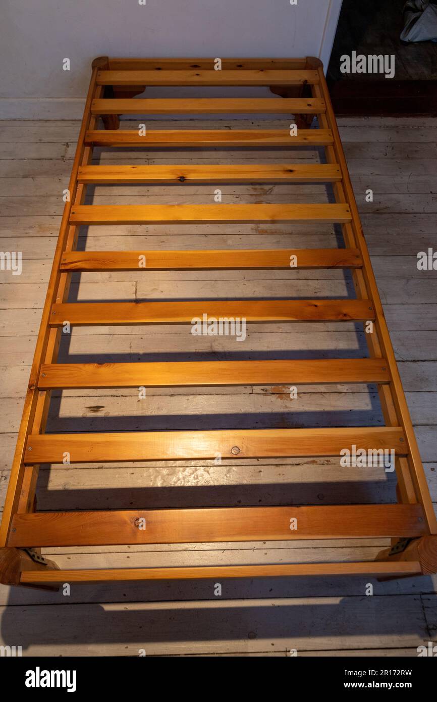 A wooden single bed in a small room with a red door white washed ...