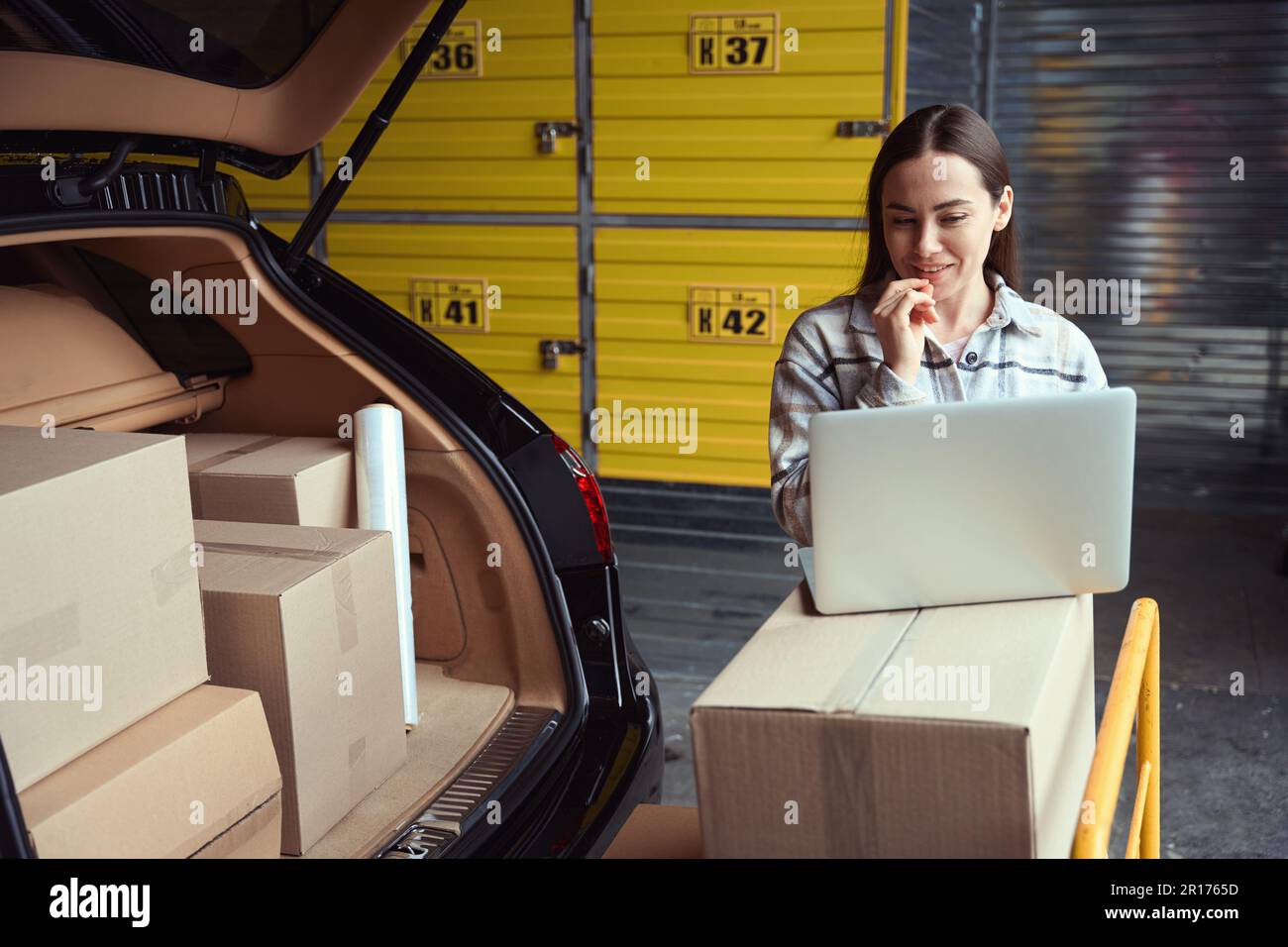 Young pleasant woman standing behind her laptop in the warehouse Stock ...
