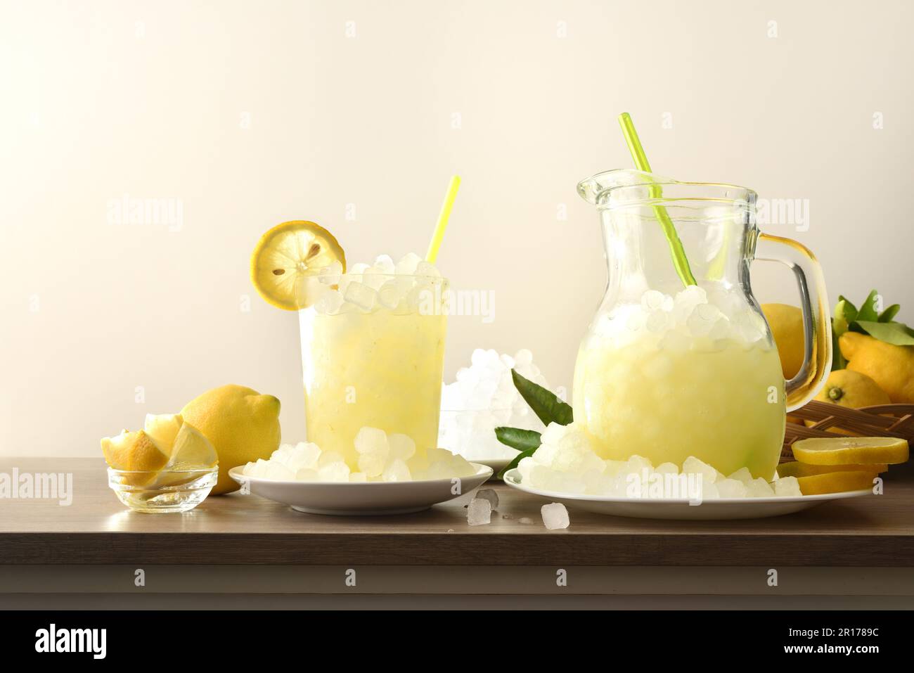 Lemonade with ice in a pitcher and glass on a wooden kitchen bench with ...