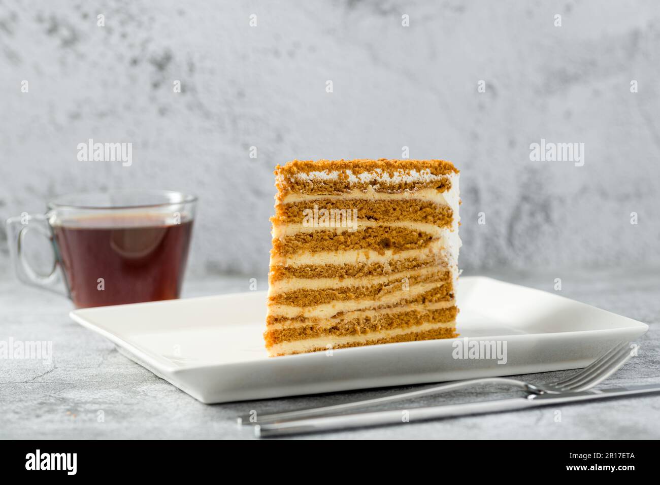 Layered honey cake slice on white porcelain plate on stone background ...
