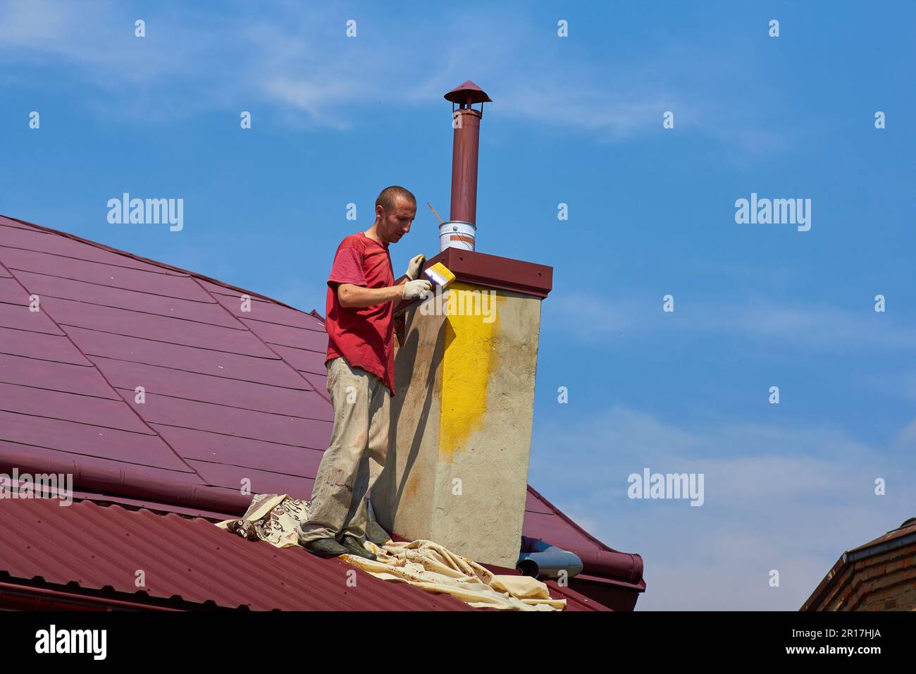 work of a painter on the roof, a man paints a brush yellow color ...