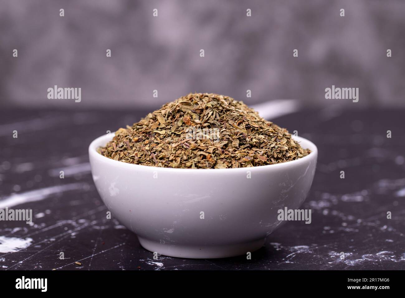 Dried crushed basil on dark background. Dried ground basil powder spices in ceramic bowl. Spice ...