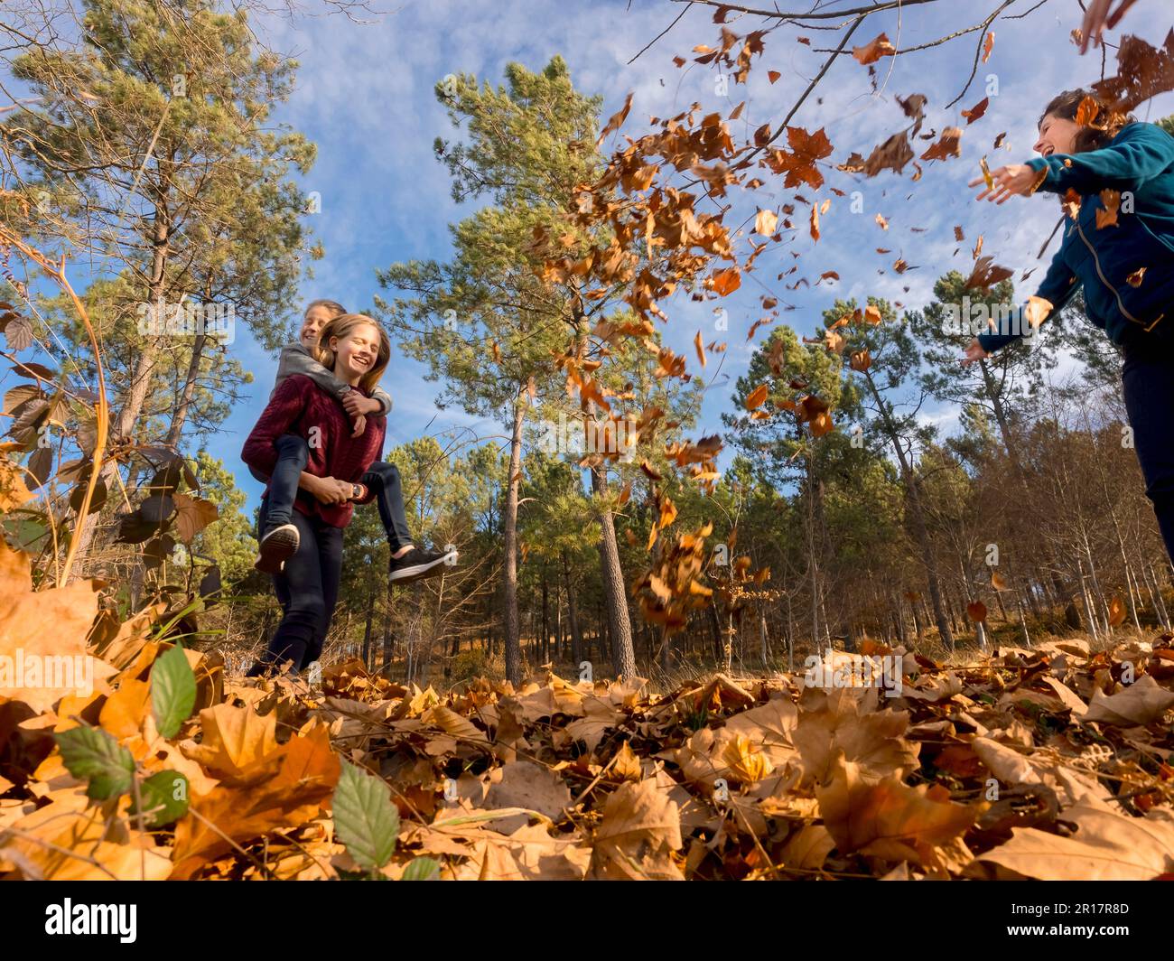 Mother standing and teenage girl carrying sister piggyback in forest ...
