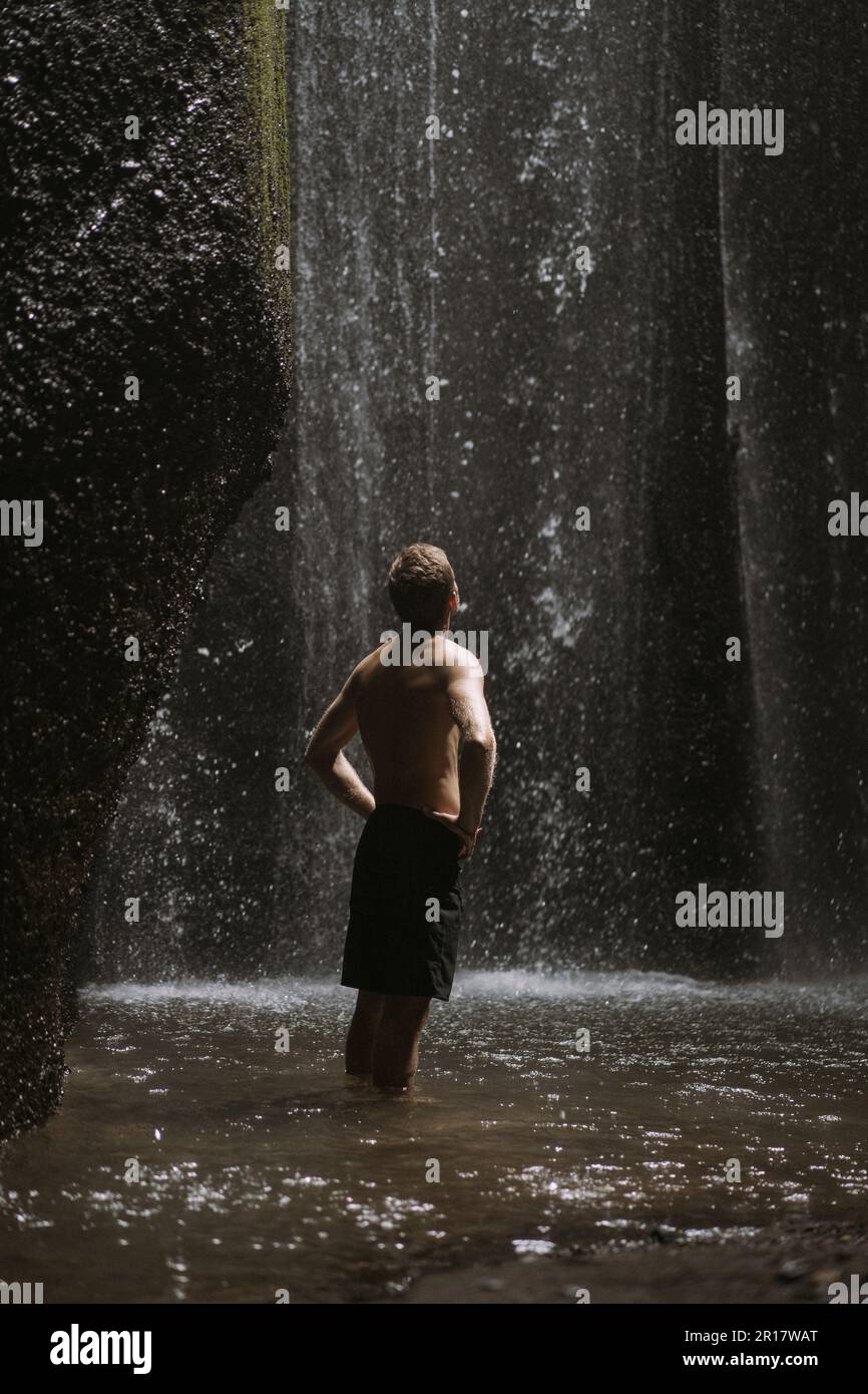 A man in a cave looks at a waterfall. Bali Stock Photo - Alamy