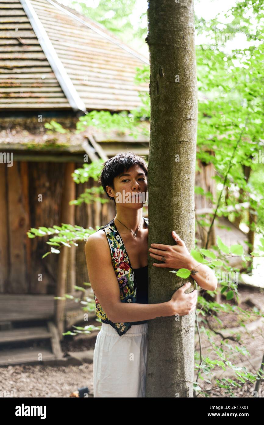 strong androgynous asian woman embraces tree by wooden house Stock ...