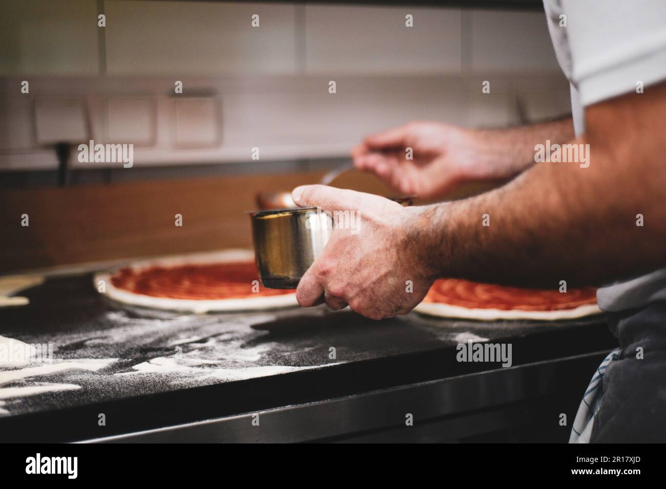 Chef hand adds tomato sauce to pizza dough in kitchen Stock Photo - Alamy