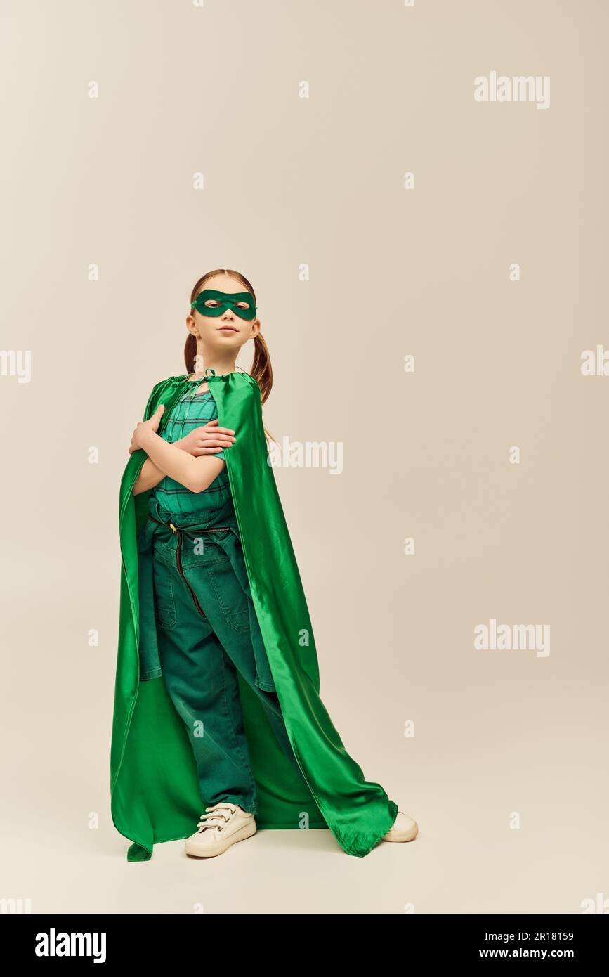 serious girl in green superhero costume with cloak and mask on face ...