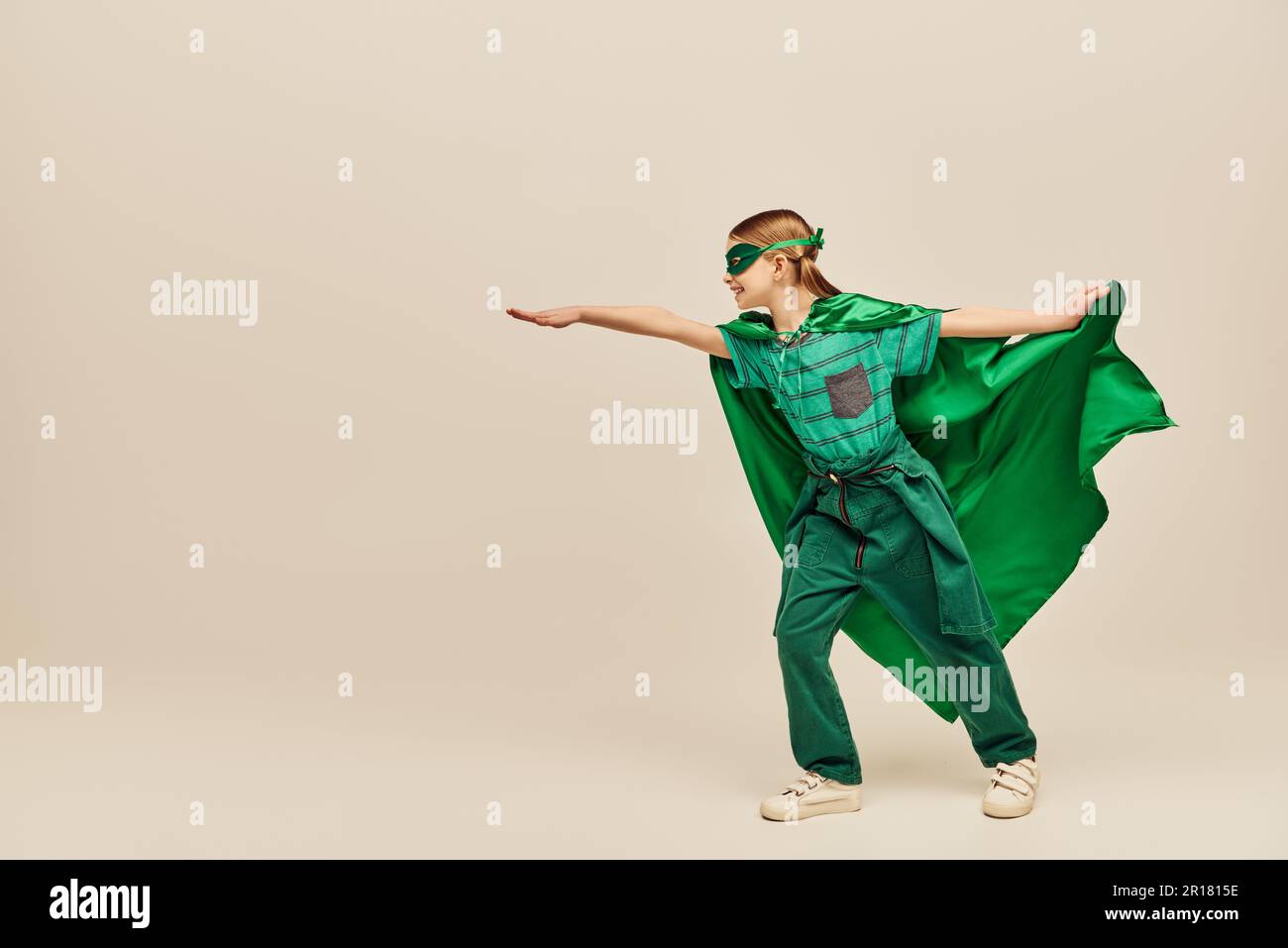side view of happy kid in superhero costume and mask holding green ...
