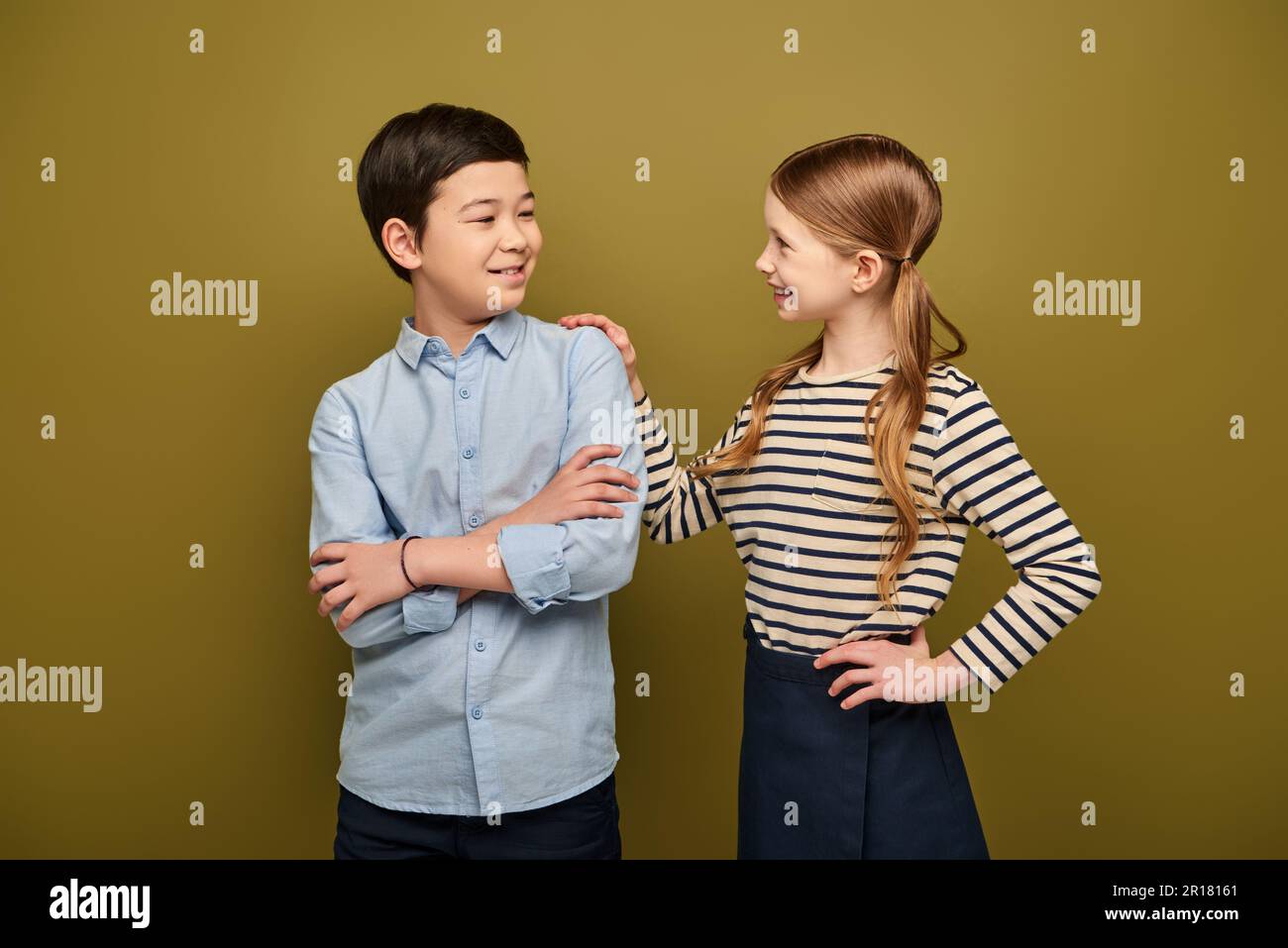 Smiling redhead preteen girl hugging and looking at asian friend ...