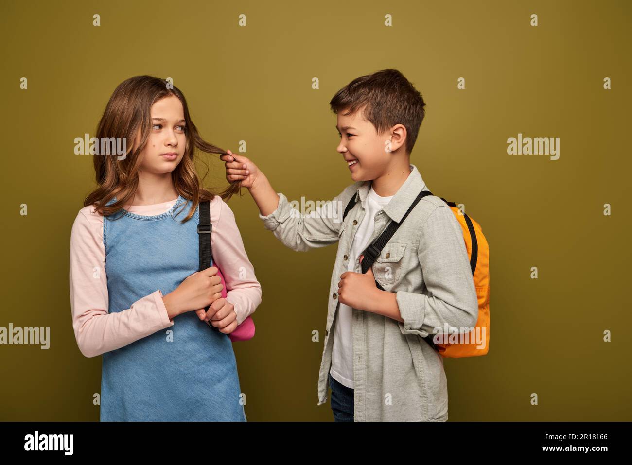 Smiling multiracial boy with backpack pulling hair of preteen girl ...