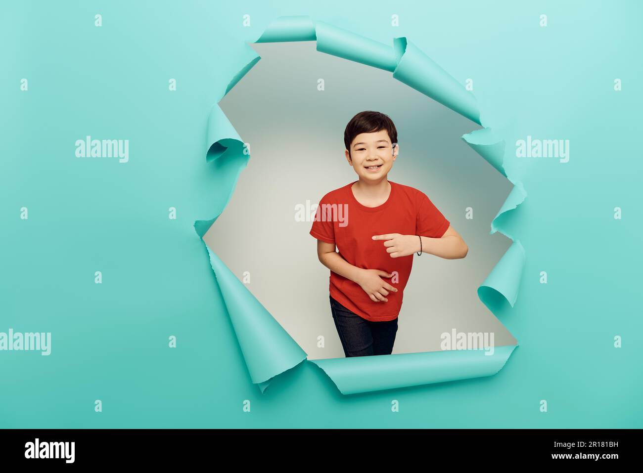 positive asian preteen boy in red t-shirt pointing with finger during ...