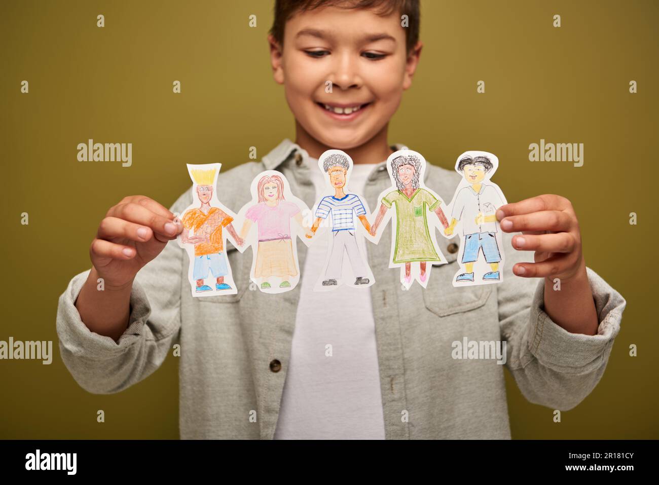 Blurred and positive multiracial boy holding drawn paper characters ...