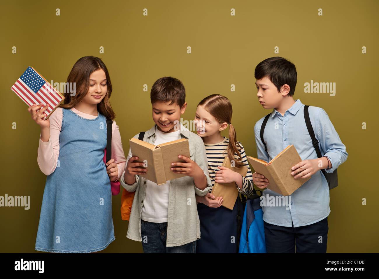 Smiling multiethnic kids with backpacks looking at multiracial friend ...
