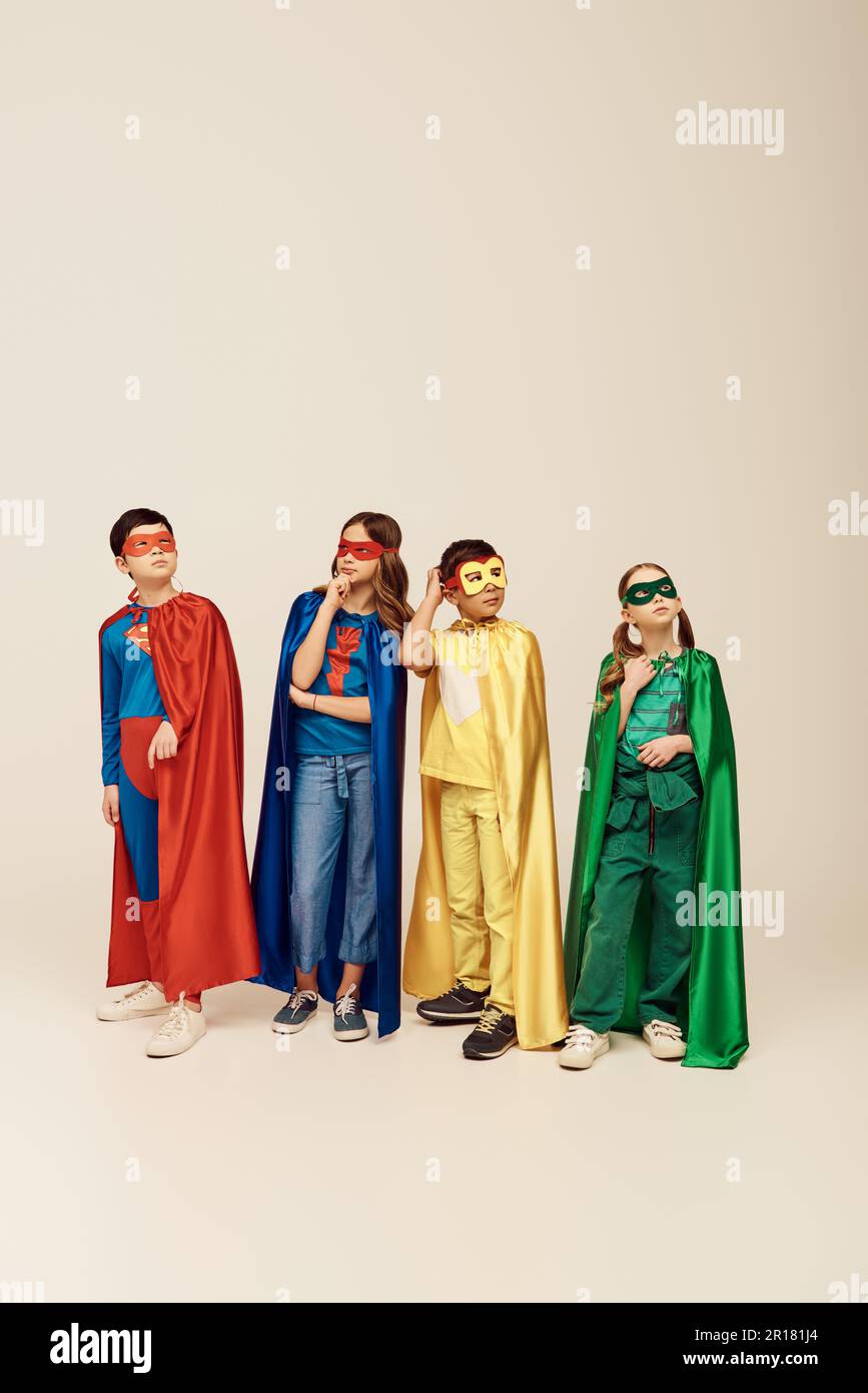 pensive multicultural kids in colorful superhero costumes with cloaks ...