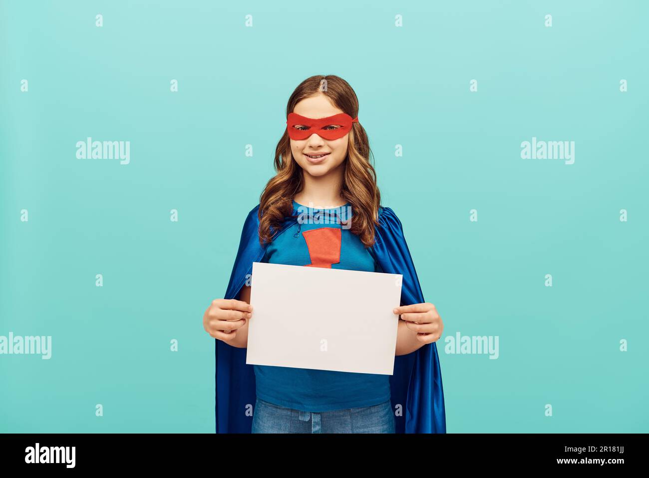 positive preteen girl in superhero costume with red mask standing with ...