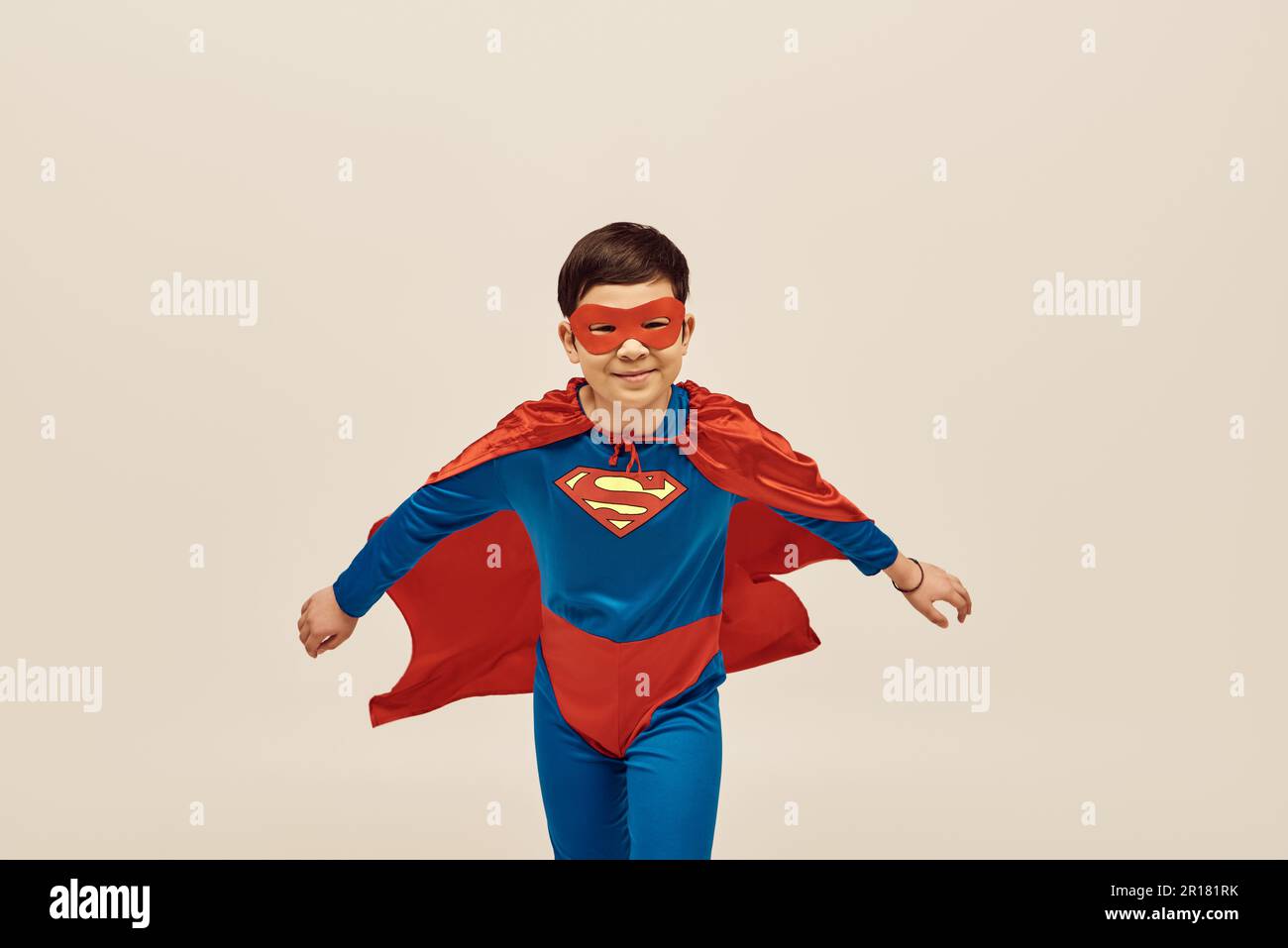 happy asian boy in red and blue superhero costume with cloak and mask ...