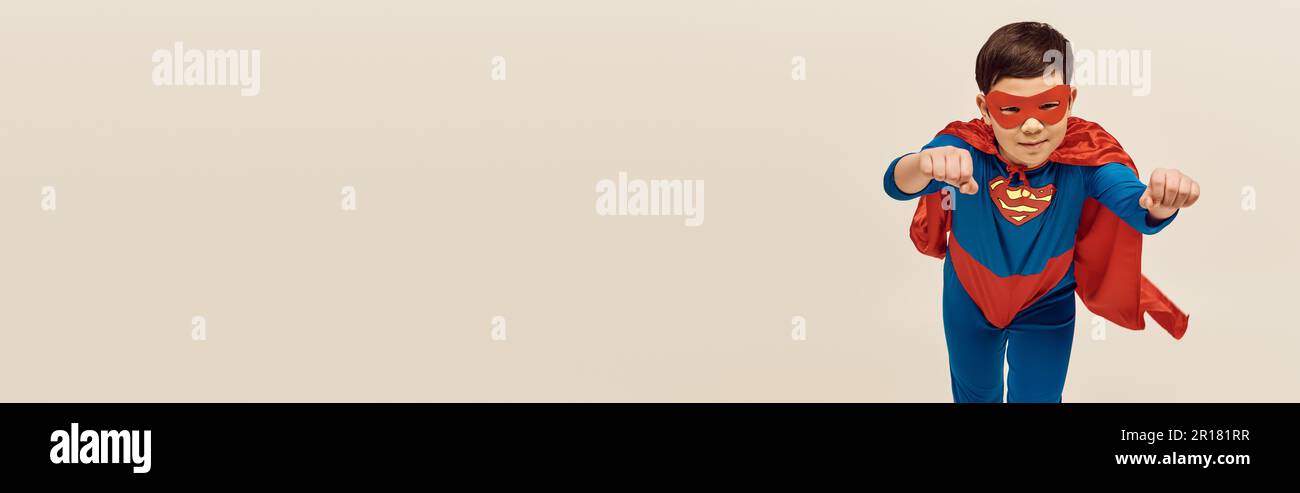 courageous asian boy in superhero costume with cloak and mask standing ...