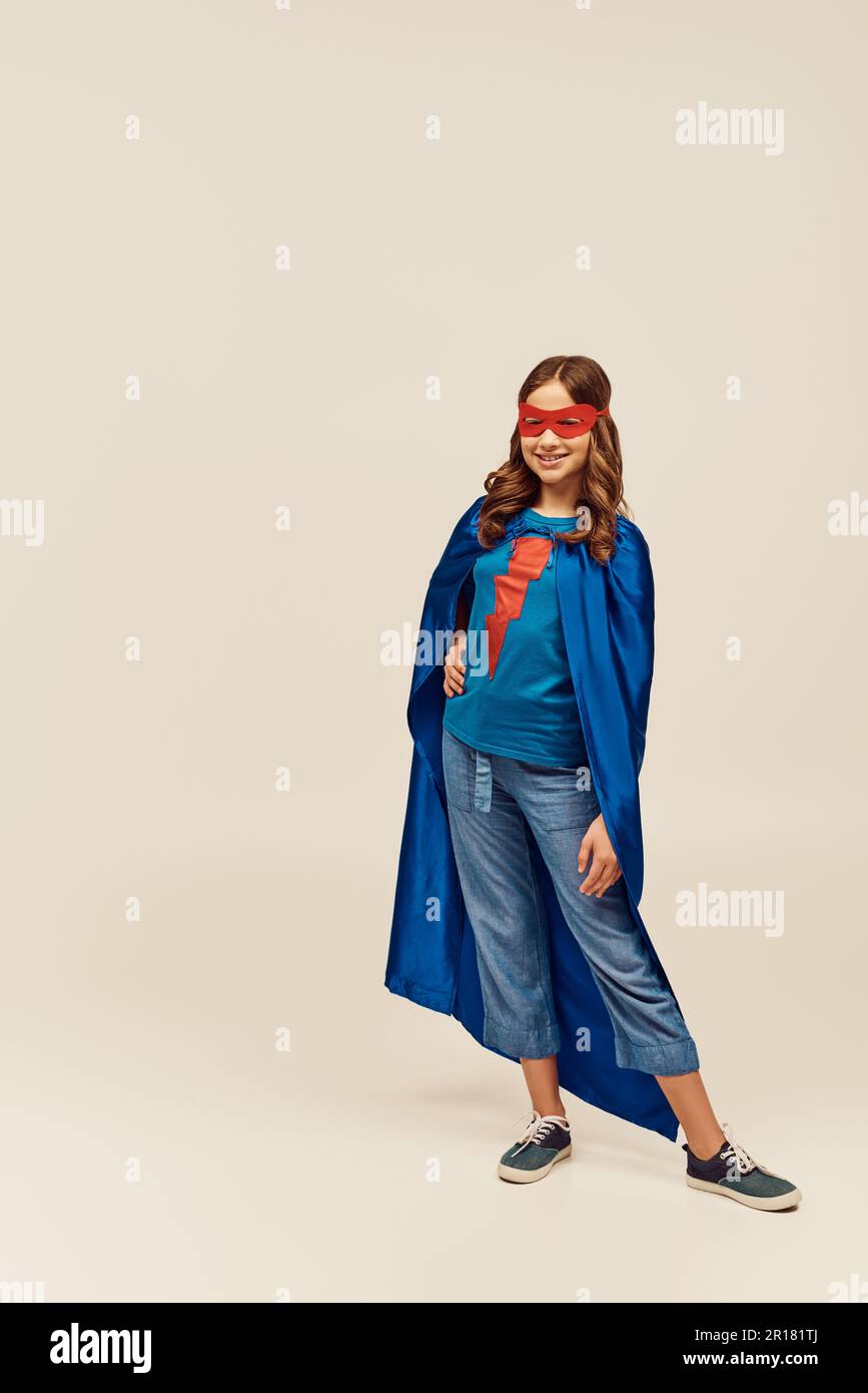 happy girl in superhero costume with blue cloak and red mask, standing ...