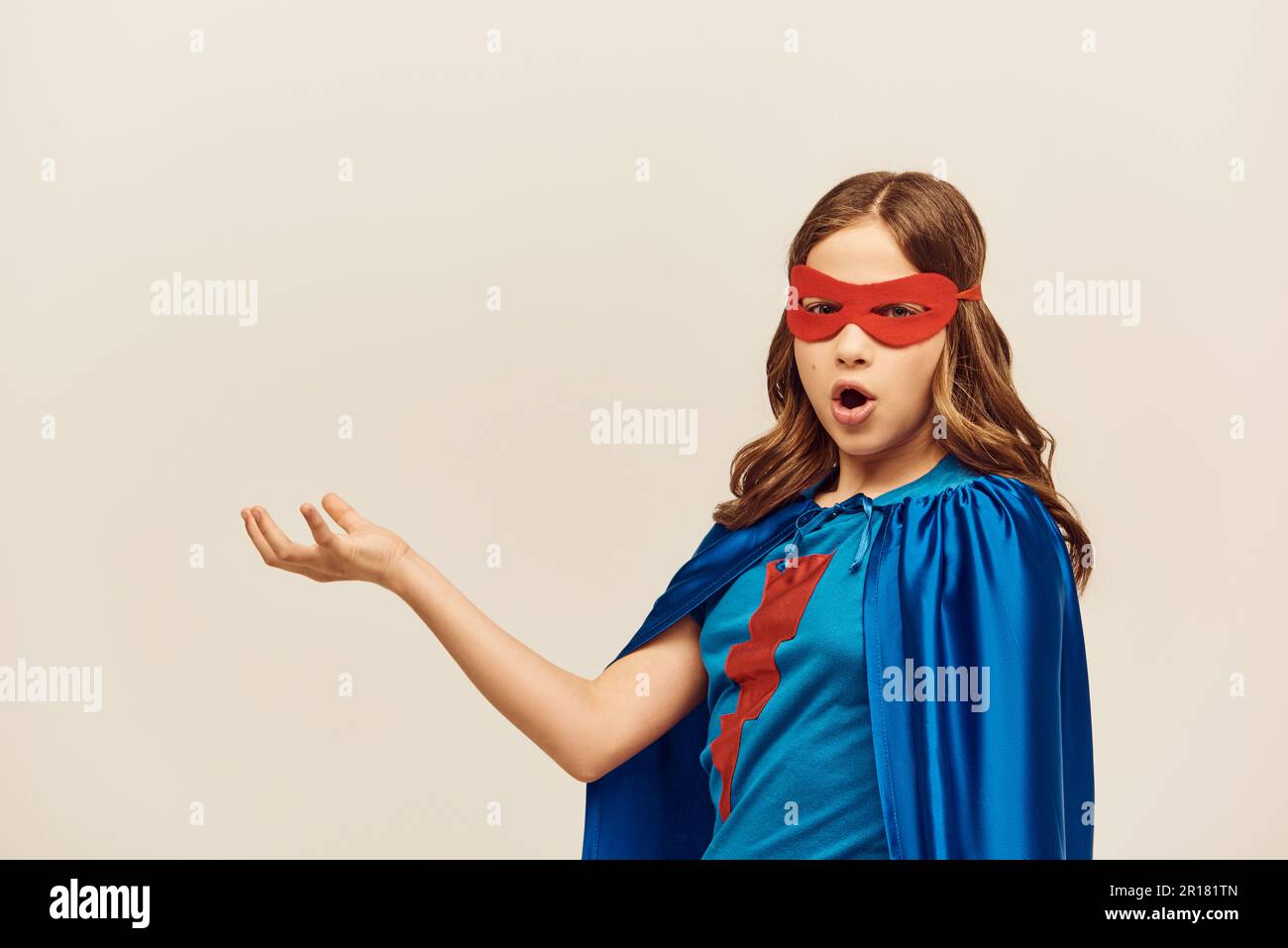 shocked superhero girl in costume with blue cloak and red mask standing ...