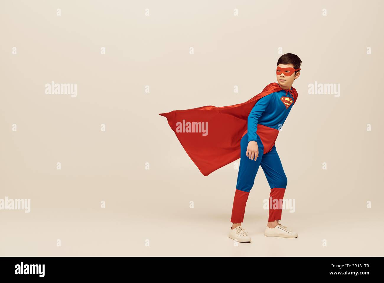 full length of courageous asian boy in superhero costume with cloak and ...