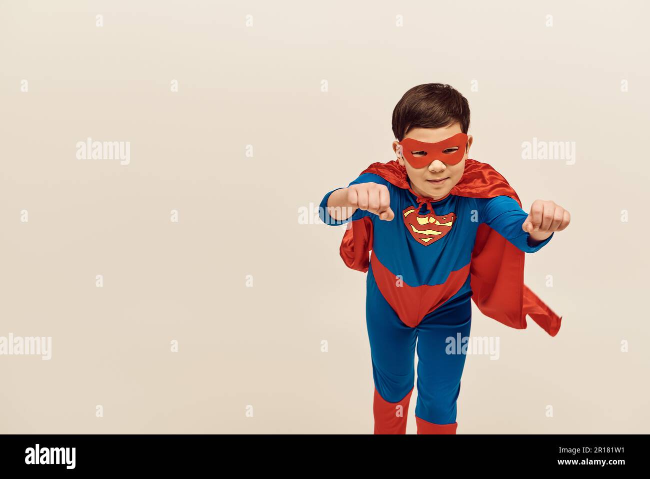 courageous asian boy in superhero costume with cloak and mask standing ...