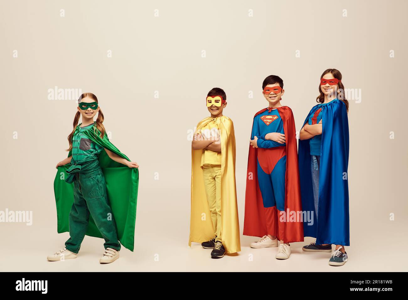 happy girl standing in green cloak and mask near interracial preteen ...