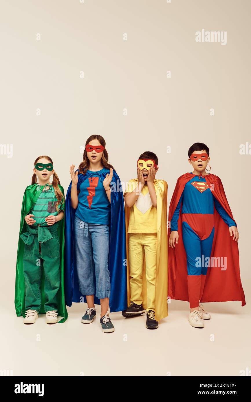 shocked interracial children in colorful superhero costumes with cloaks ...
