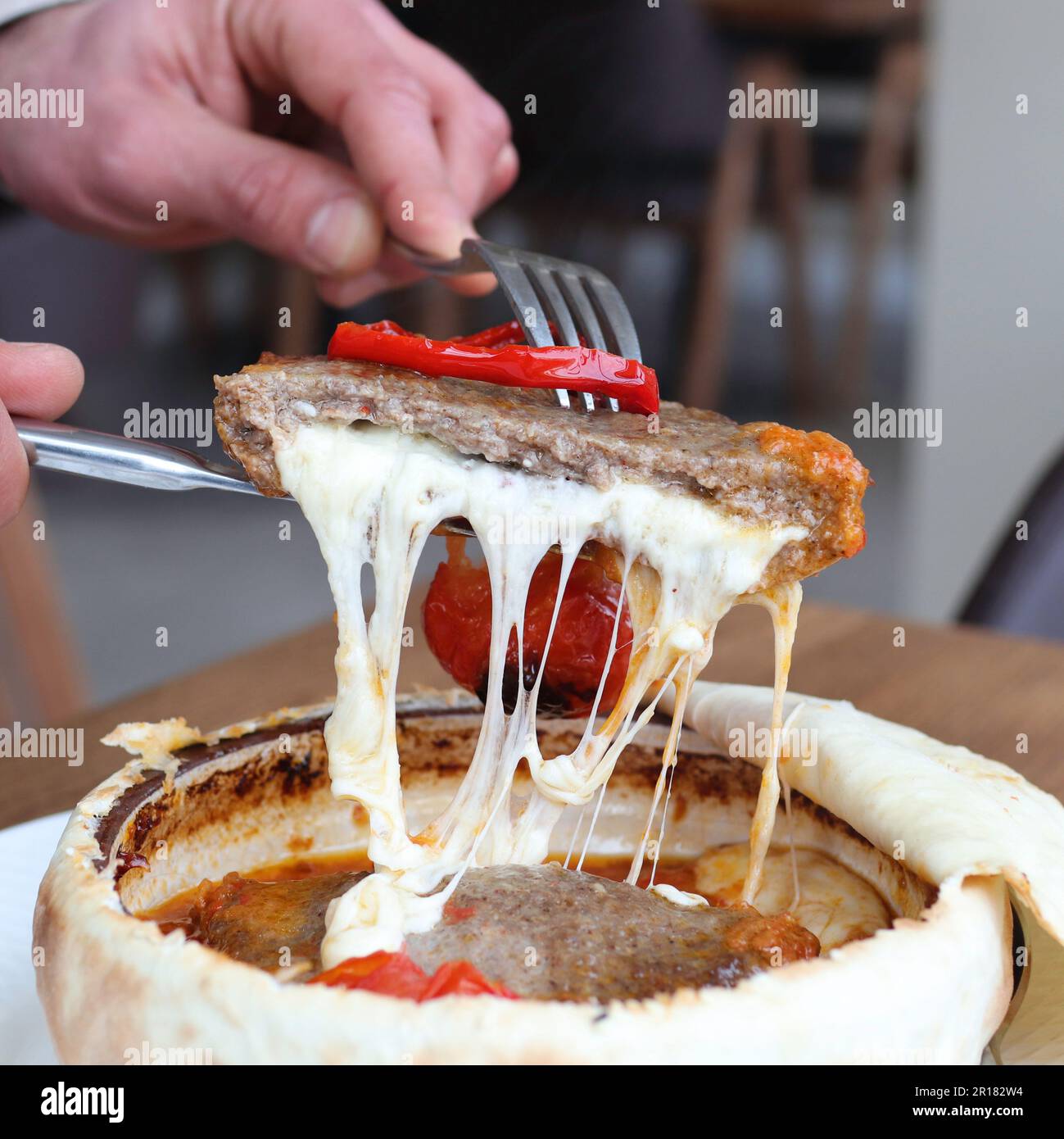 A close-up of a man holding a fork, pulling out a slice of meat topped ...