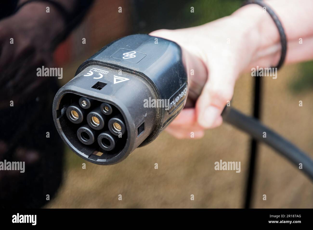 A hand holding a connector to plug in and charge an electric vehicle ...