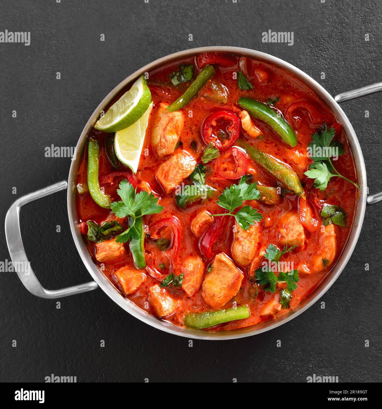 Thai style red chicken curry with vegetables in pan over black stone ...