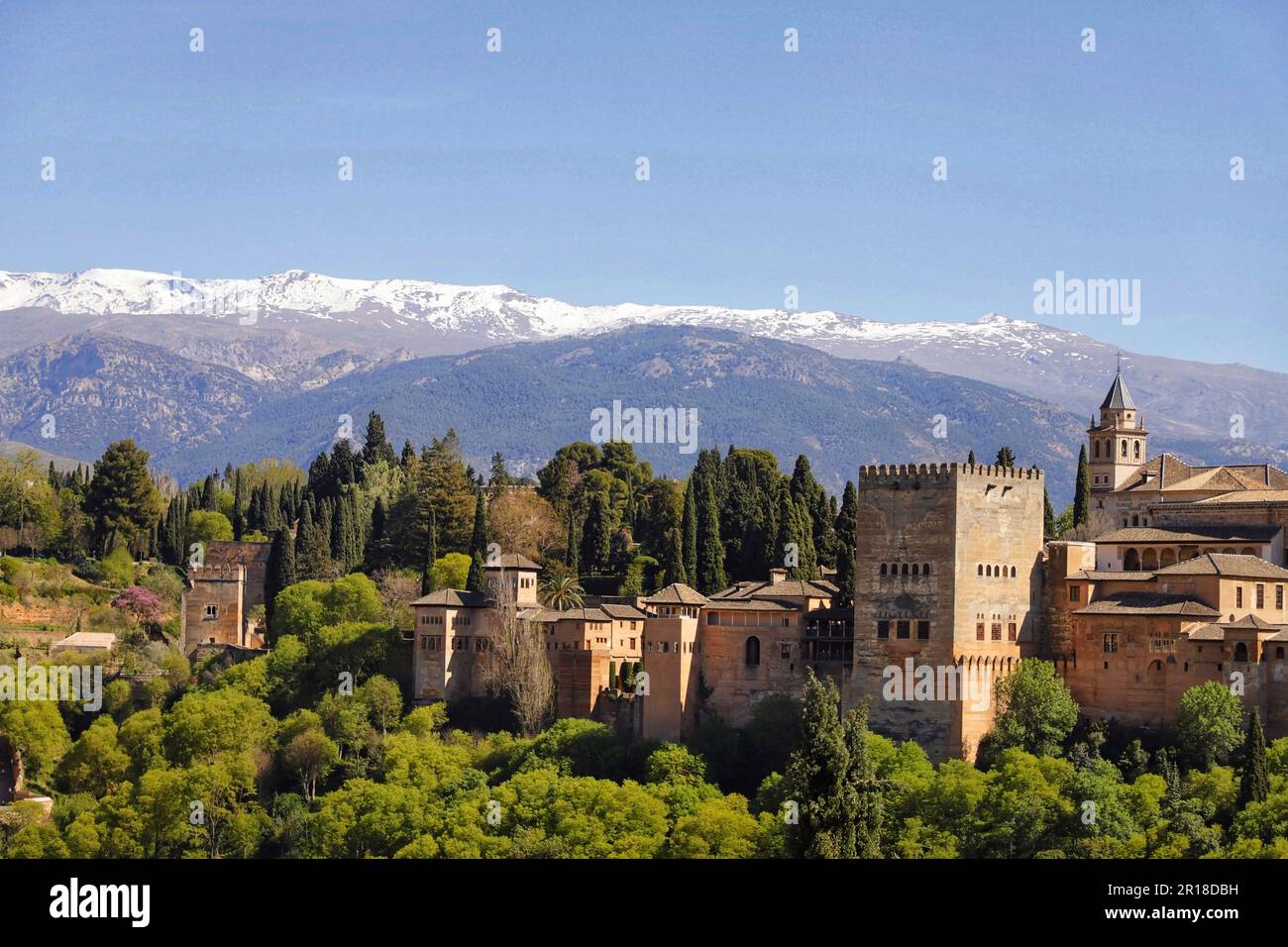The majestic Alhambra castle towers over a lush forest landscape, and ...