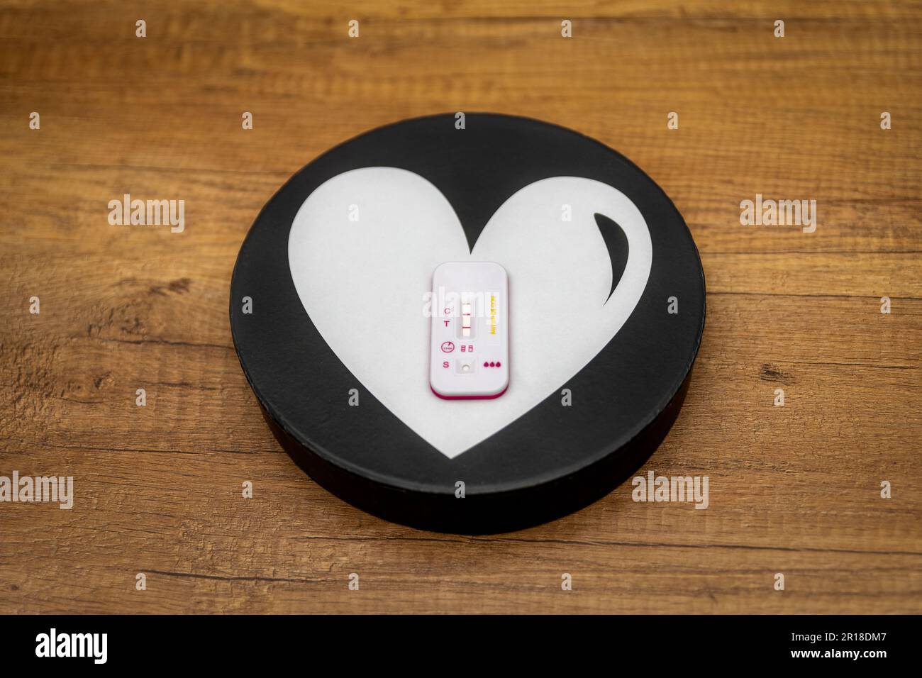 The image shows a heart-shaped box with a positive pregnancy test ...