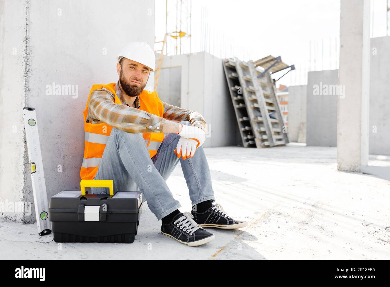 Builder repairman, foreman in safety helmet and vest sitting down to ...