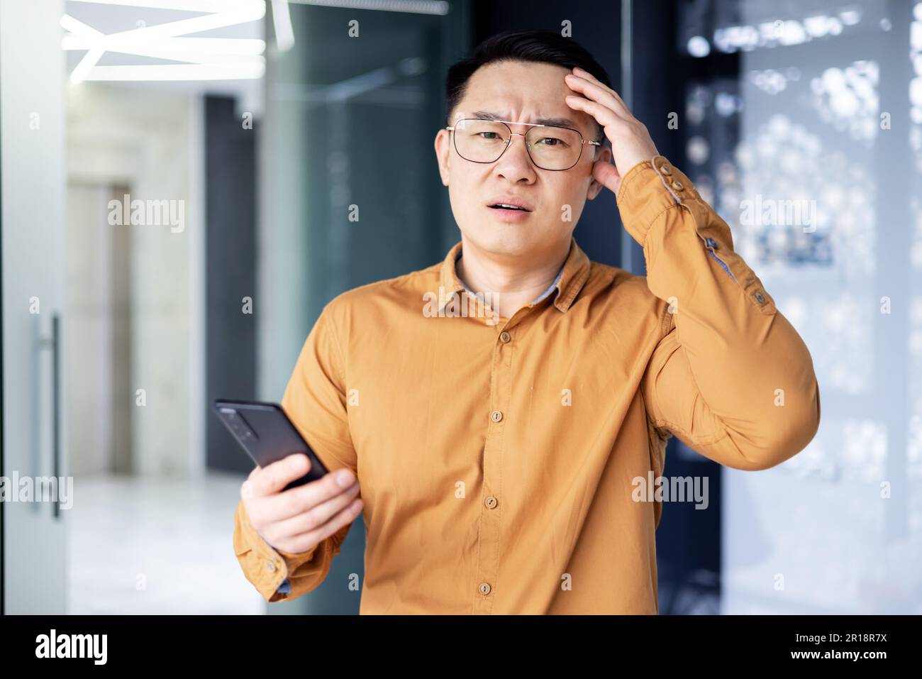 Dissatisfied Asian looking at camera, man inside office holding phone ...