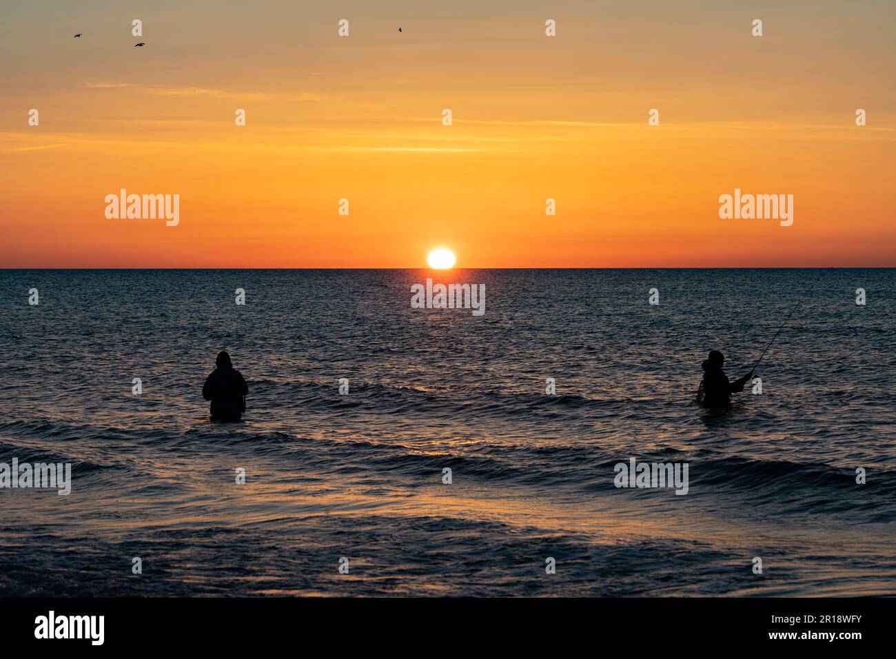The silhouettes of two anglers in waterproof trousers fishing in front ...