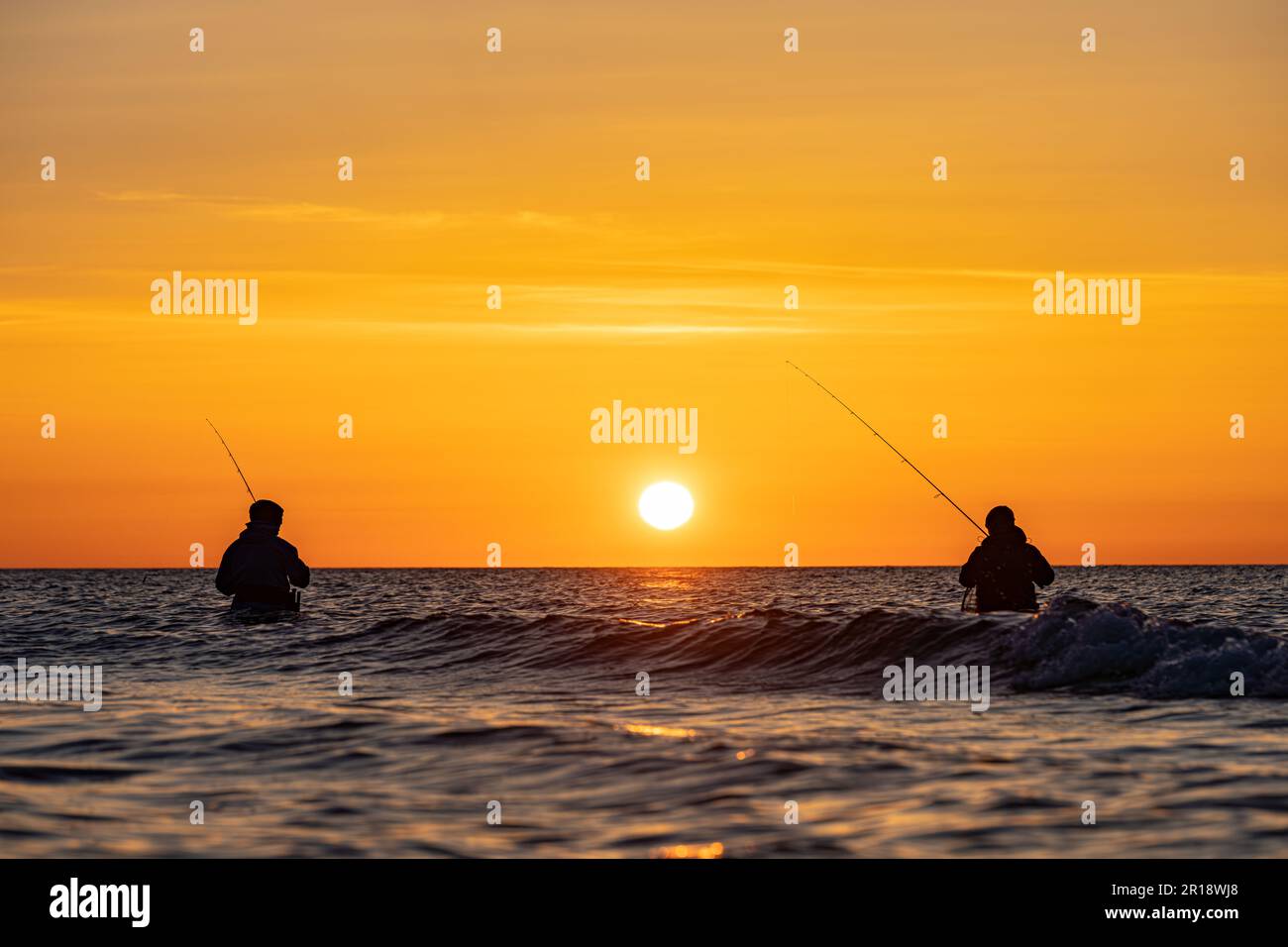 The silhouettes of two anglers in waterproof trousers fishing in front ...